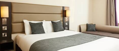 Quarto de hotel com uma cama grande, um sofá e uma mesa de cabeceira com luminária.