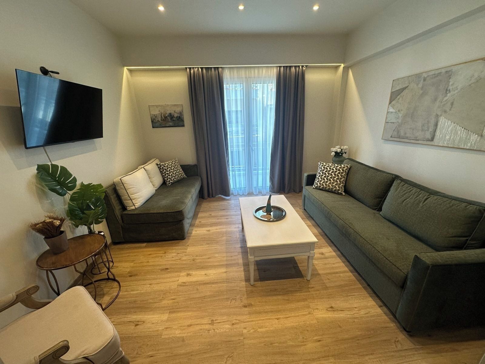 Uma sala de estar moderna com televisão de tela plana, dois sofás, uma mesa de centro e uma janela grande com cortinas.