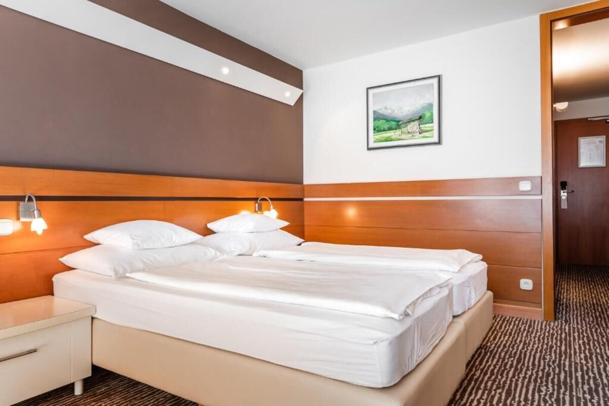 Quarto de hotel com cama de casal, mesas de cabeceira, luminária fixada na parede e um quadro emoldurado.