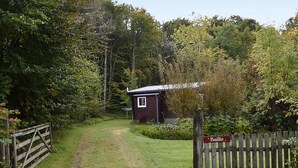 Uma propriedade rural com um portão de madeira, um pequeno edifício com a placa 'Baillie' e um caminho gramado que o conduz.