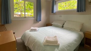 Quarto com cama, duas janelas com cortinas, mesa de cabeceira e criado-mudo.