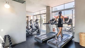 Uma academia com esteiras, halteres e uma janela grande com vista para a cidade.