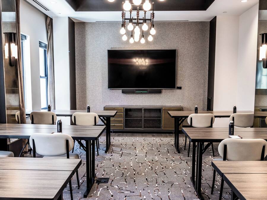 Uma sala de conferências com uma grande televisão de tela plana, várias mesas, cadeiras, um tapete estampado e um candelabro.