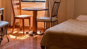Quarto com uma cama, duas cadeiras, uma mesinha e uma janela com cortinas.
