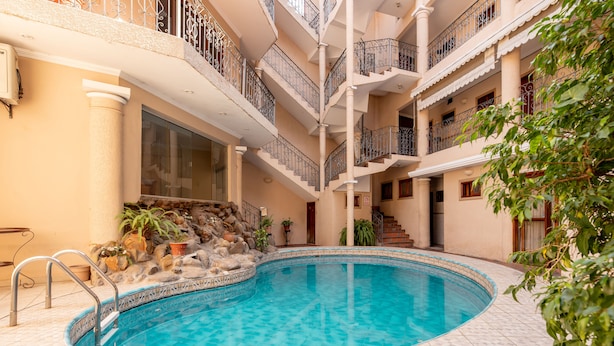 Uma piscina interior em vários níveis, com chão em mosaico, rodeada por varandas com grades de metal e uma parede de pedra com plantas.