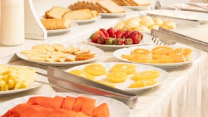 Uma mesa de buffet com diversos alimentos, incluindo frutas, pães e bebidas.