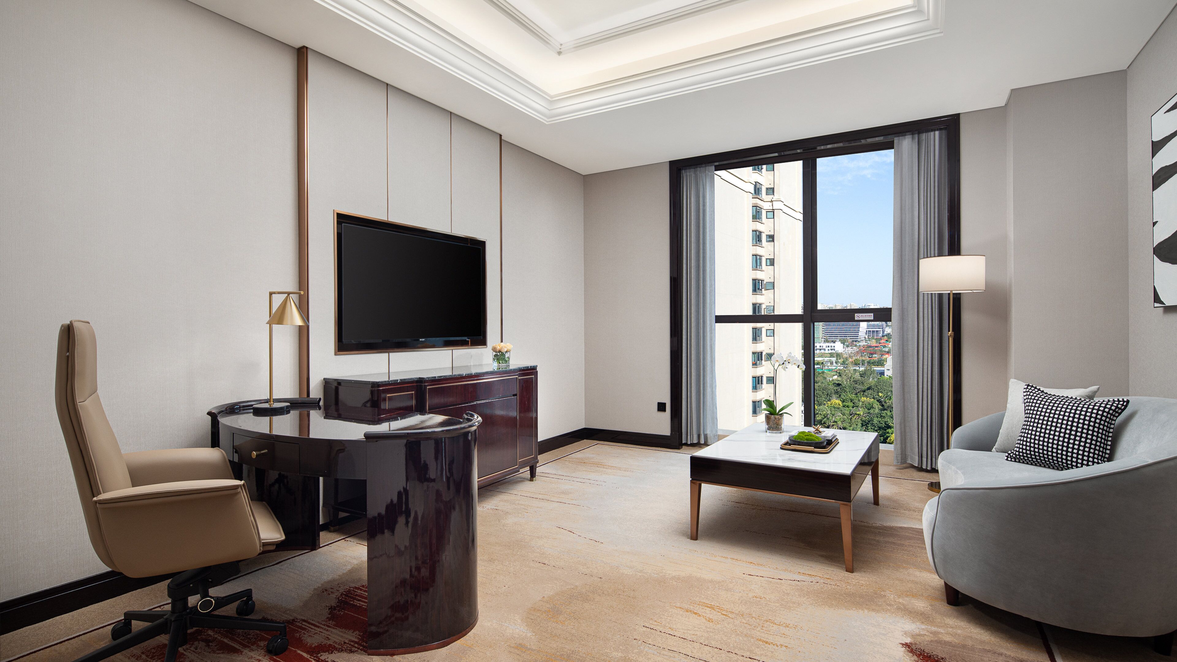 Quarto de hotel moderno com uma TV grande, uma escrivaninha, um sofá e vista da cidade por grandes janelas.
