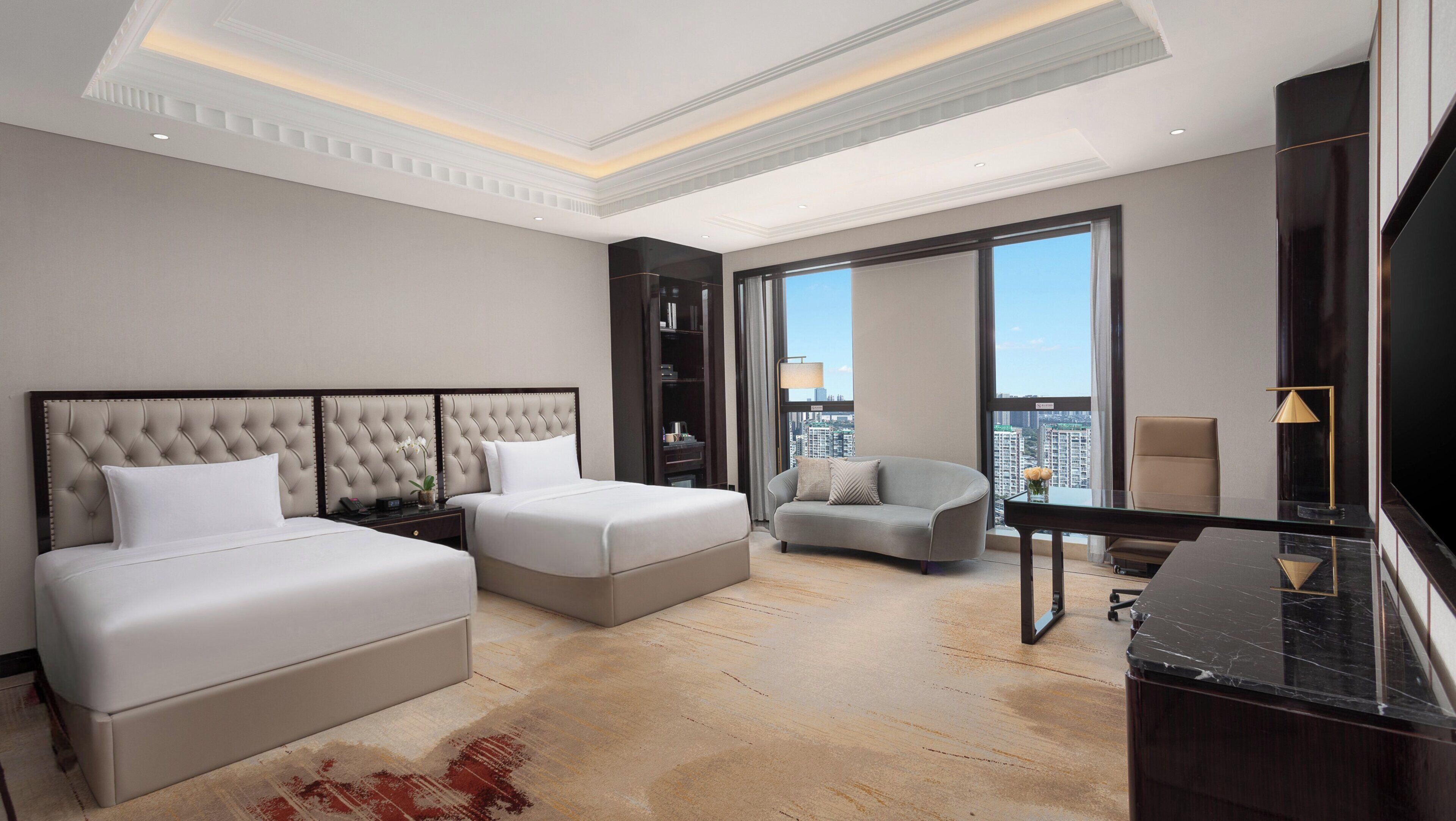 Quarto de hotel com uma cama grande, uma cama menor, um sofá, uma escrivaninha e uma televisão.