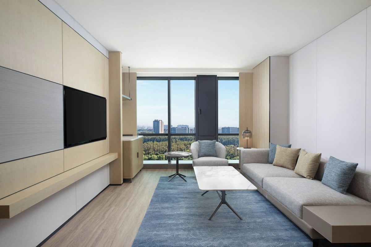 Uma sala de estar moderna com uma televisão grande, um sofá, uma mesa de centro e vista para a cidade através de grandes janelas.