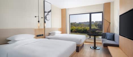 Quarto de hotel com duas camas, um sofá, uma televisão e uma grande janela com vista para a cidade.