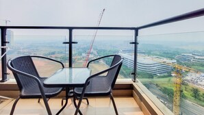 Varanda com duas cadeiras e uma mesa, com vista para um canteiro de obras com guindastes e edifícios.