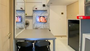 Uma cozinha moderna com painel de parede de mármore, duas televisões fixadas na parede, uma mesa de jantar com cadeiras e uma geladeira embutida.