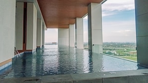 Uma piscina infinita moderna com teto de madeira e grades de vidro, proporcionando vista para o horizonte da cidade.