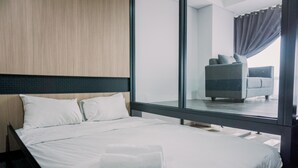 Quarto de hotel moderno com uma cama grande, vista para outro quarto através de uma parede de vidro e uma janela com cortinas.