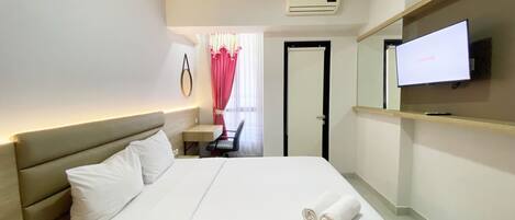 Quarto de hotel com uma cama, uma escrivaninha, uma cadeira, uma televisão e uma porta.