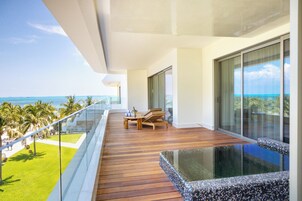 Uma varanda com piso de madeira, guarda-corpo de vidro e vista para o oceano.