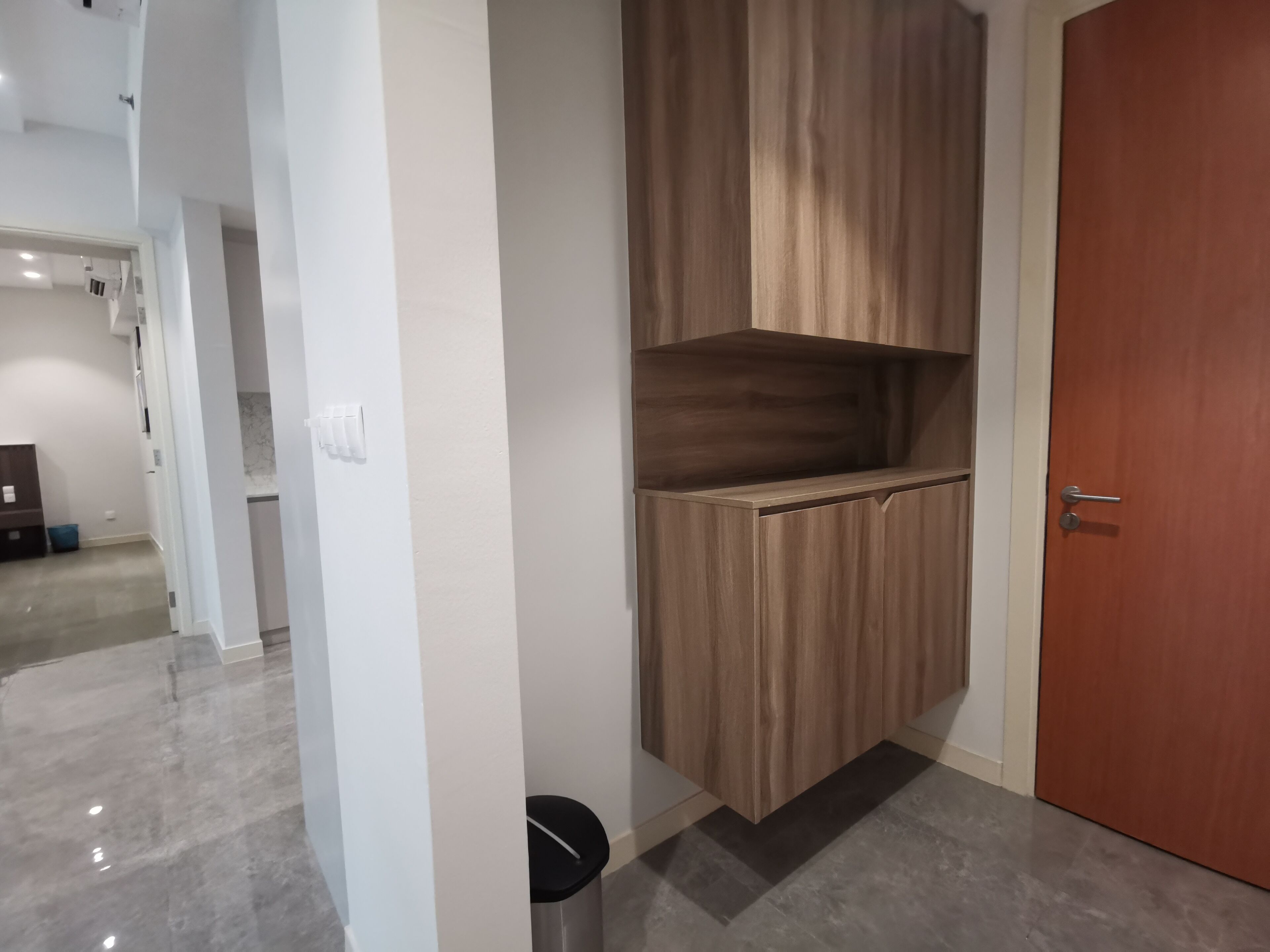 Um corredor com um armário de madeira, uma lixeira e uma porta.