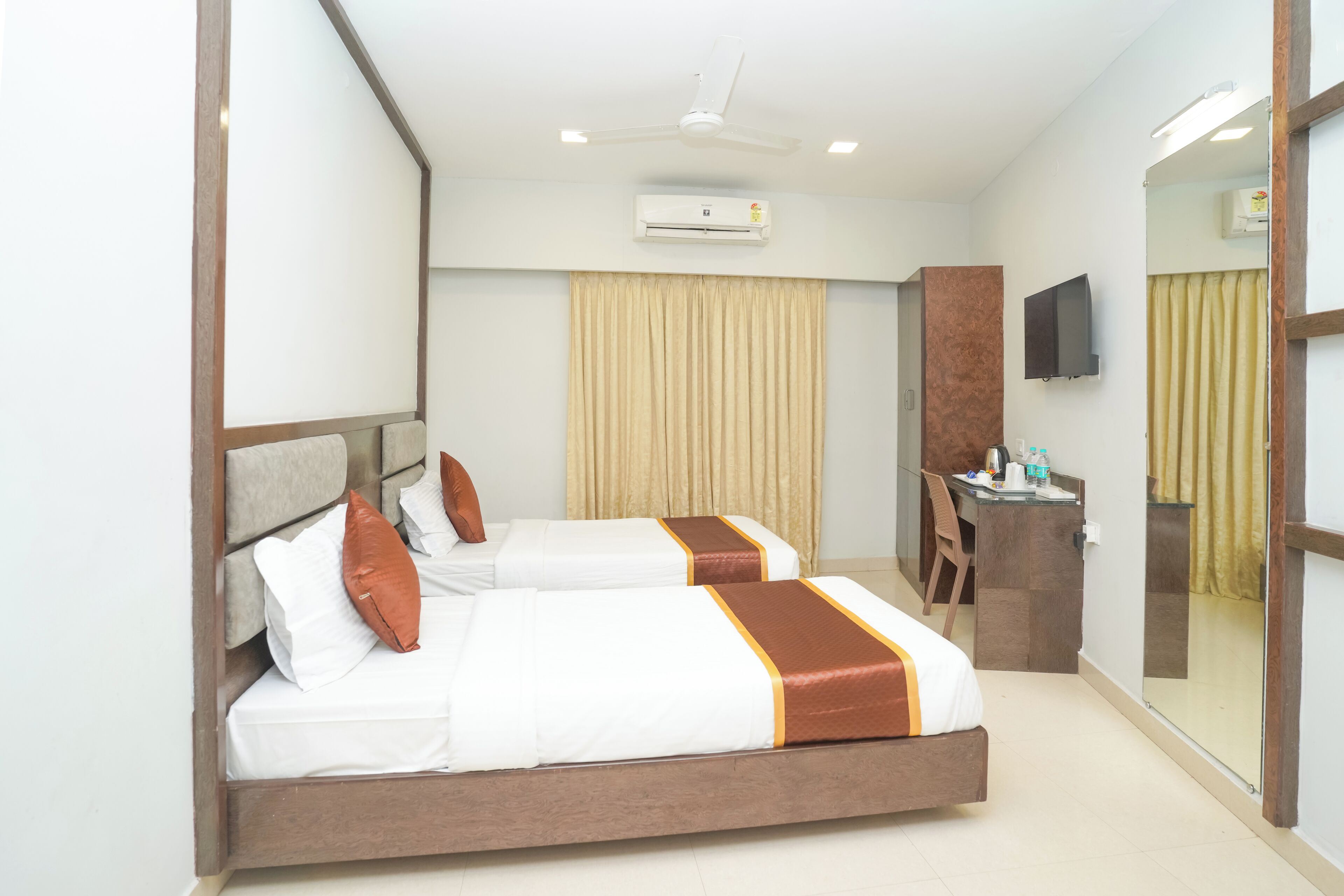 Quarto de hotel com duas camas, uma escrivaninha, uma cadeira, ar condicionado, televisão e porta de vidro deslizante.