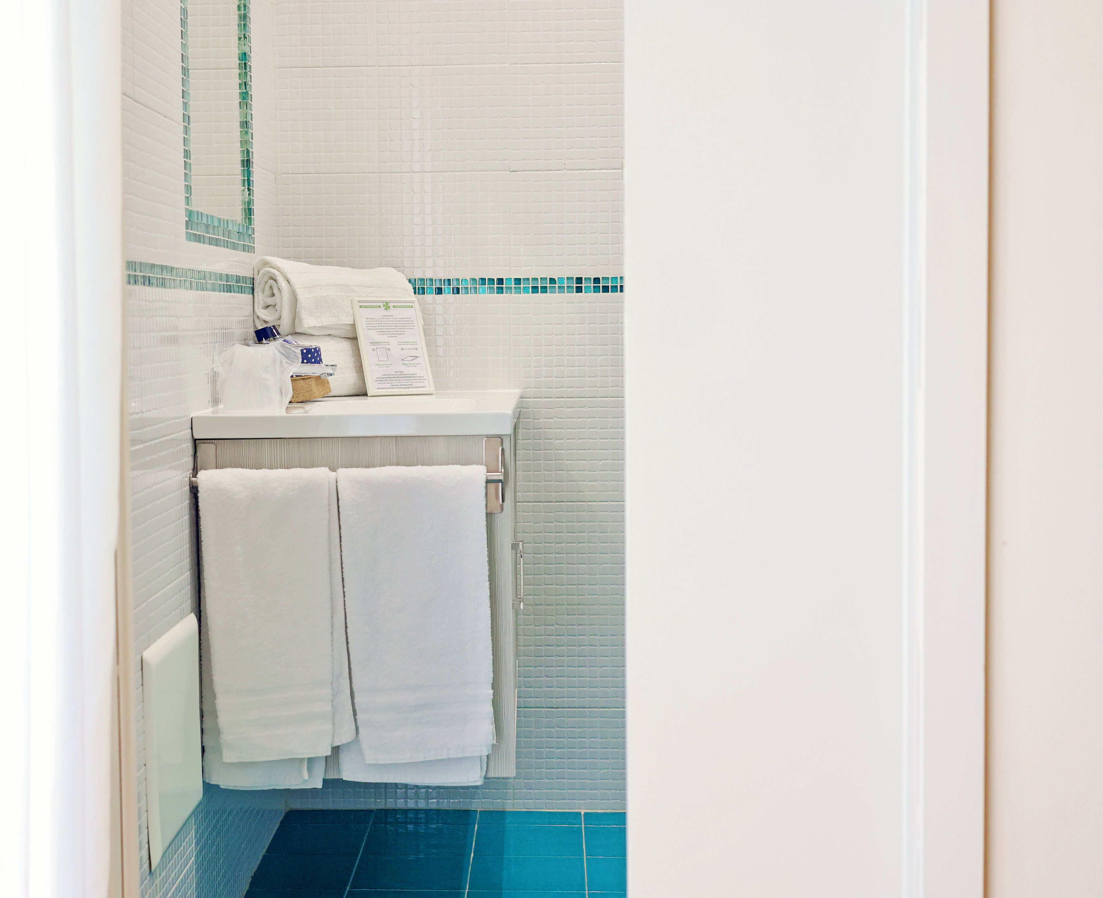 Um banheiro com paredes revestidas de azulejos brancos, piso de azulejos azuis e pia branca com um porta-toalhas com duas toalhas.