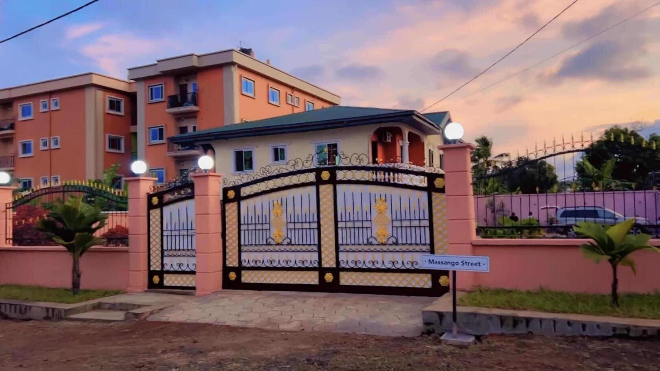 Entrada fechada por portão para um prédio residencial, com uma placa indicando 'Massango Street'.