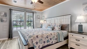 Quarto com cama, mesas de cabeceira, ventoinha no teto e janela com persianas.