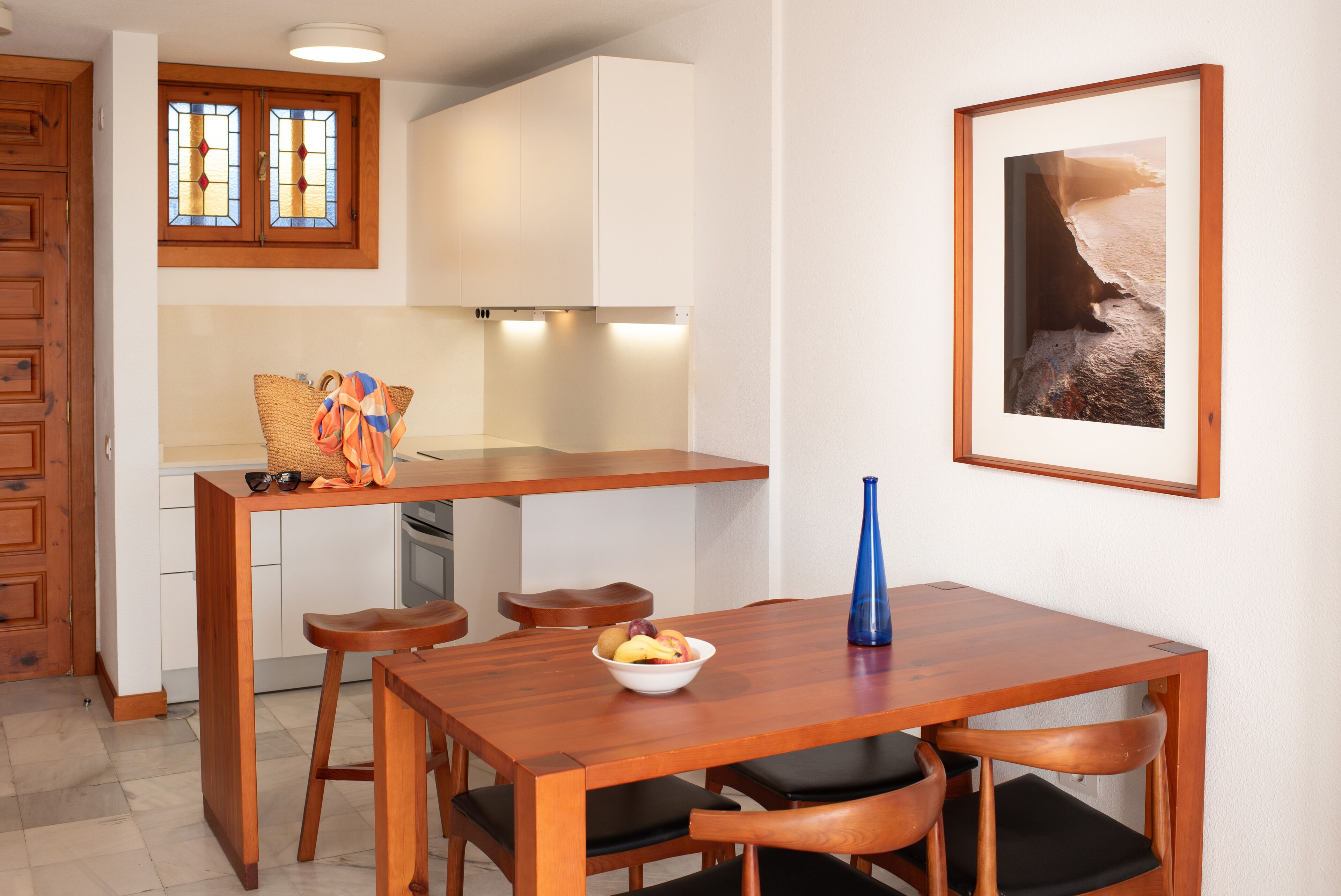 Uma cozinha compacta com armários brancos, uma mesa de jantar de madeira e um vaso azul.