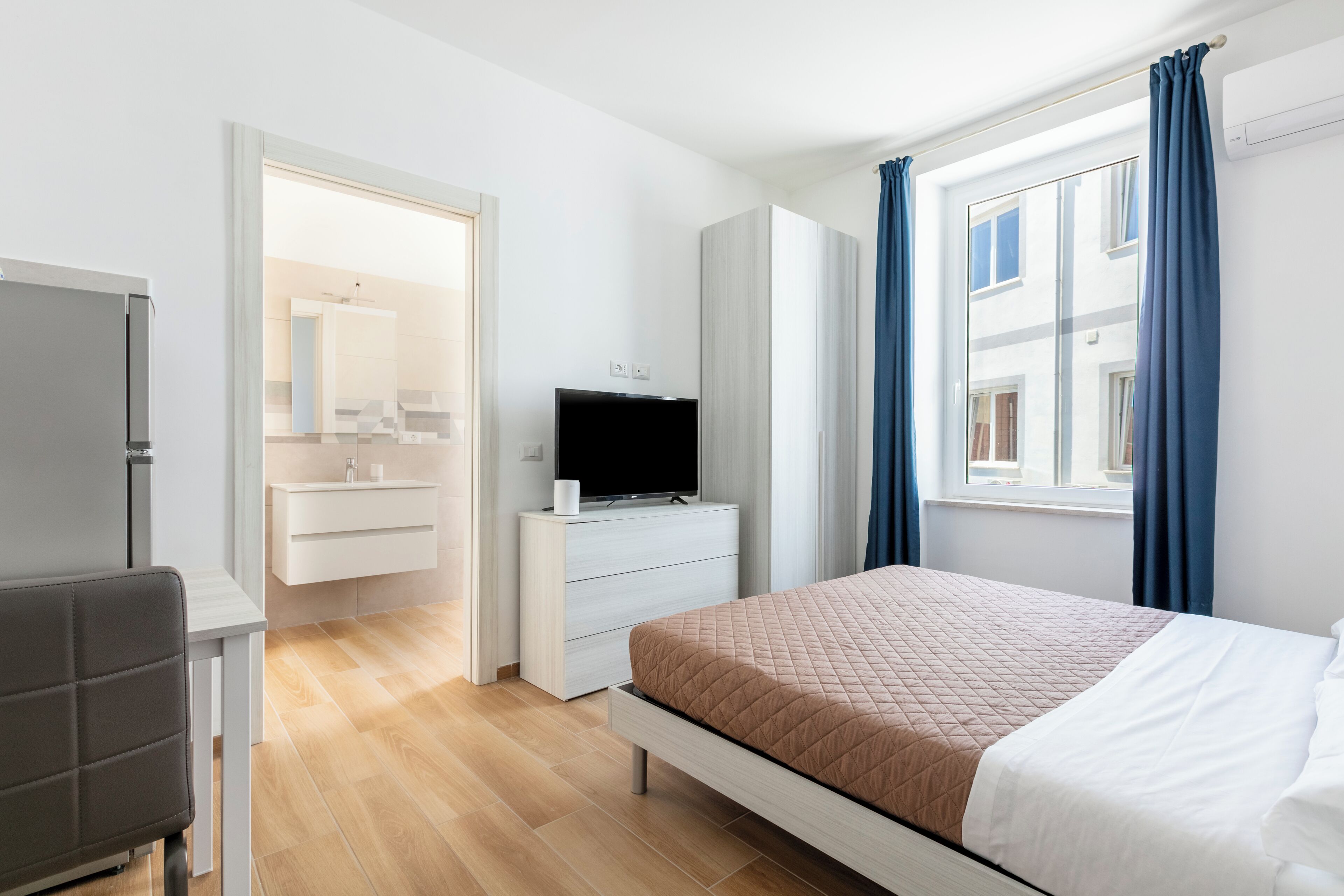Quarto de hotel moderno com cama, televisão, escrivaninha e banheiro.