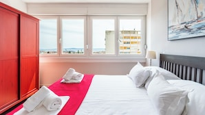 Quarto de hotel com cama, um armário vermelho e janela com vista para a cidade.