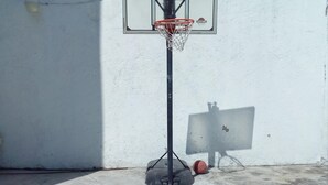 Uma tabela de basquete fixada em piso de concreto com parede branca ao fundo.