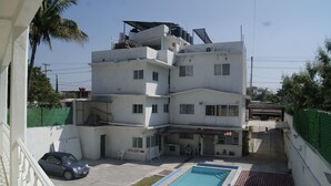 Um edifício de vários andares com piscina e um carro estacionado em frente.