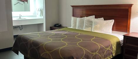 Quarto de hotel com cama, mesa de cabeceira, cômoda, espelho e banheiro com porta-toalhas.