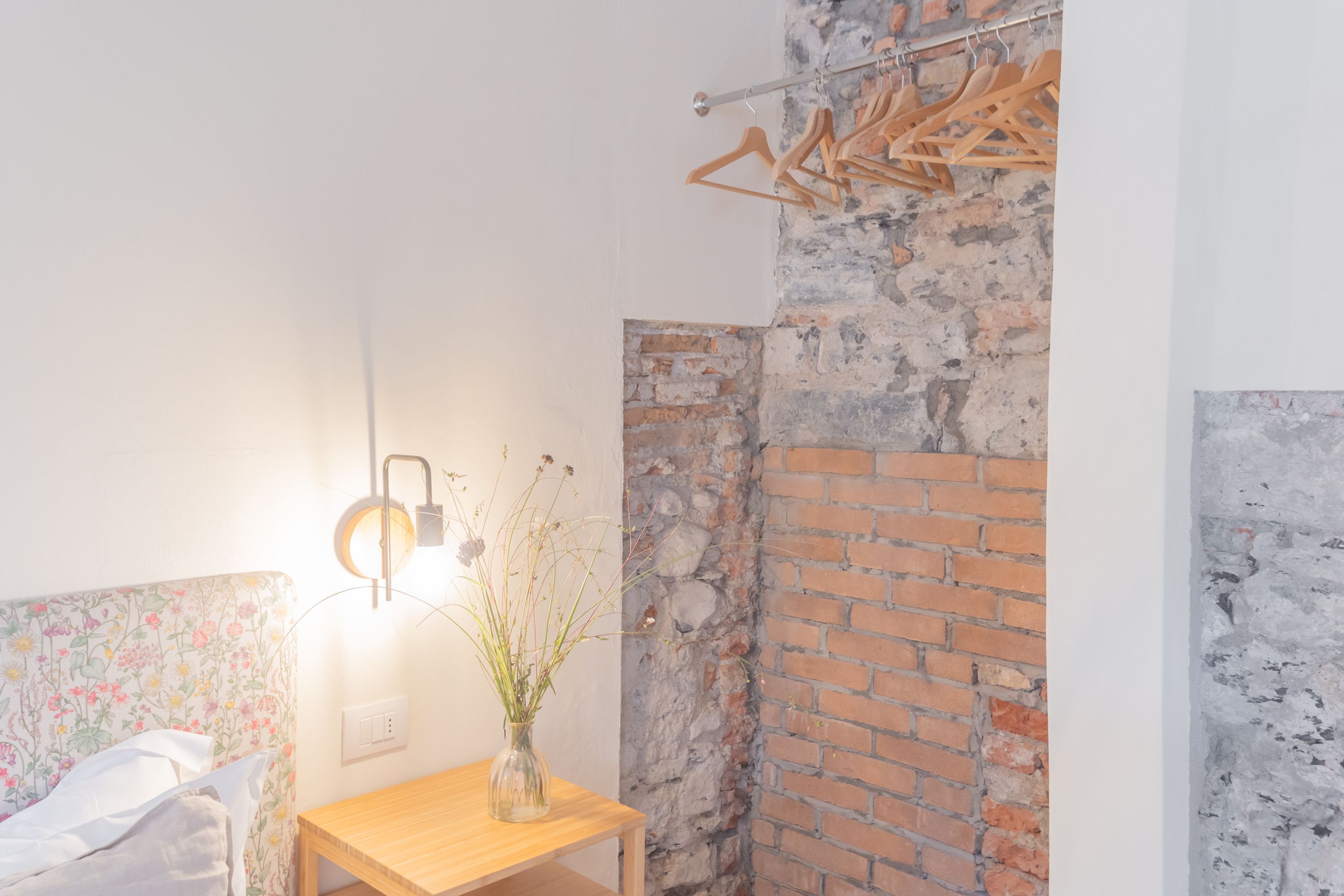Quarto com parede de tijolos, uma mesa de madeira com um vaso e uma cama com roupa de cama florida.