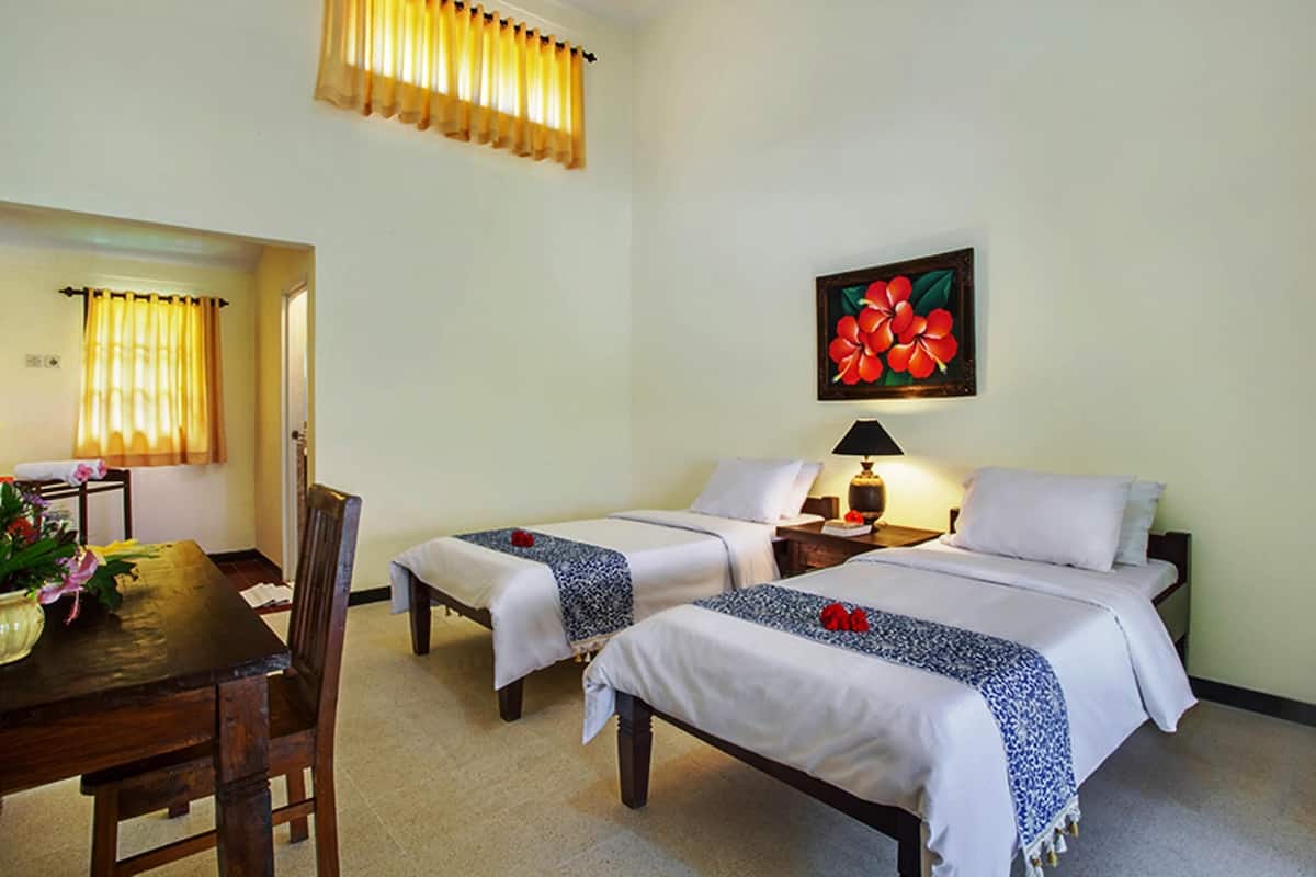Quarto de hotel com duas camas de solteiro, uma mesa de madeira, uma cadeira, uma escrivaninha e um quadro na parede.