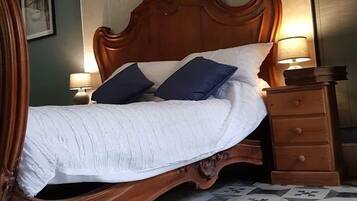 Quarto com cama de madeira, roupa de cama branca, mesa de cabeceira com abajur e piso estampado.