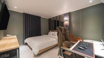 Quarto de hotel moderno com cama, secretária, computador, cadeira e televisão.