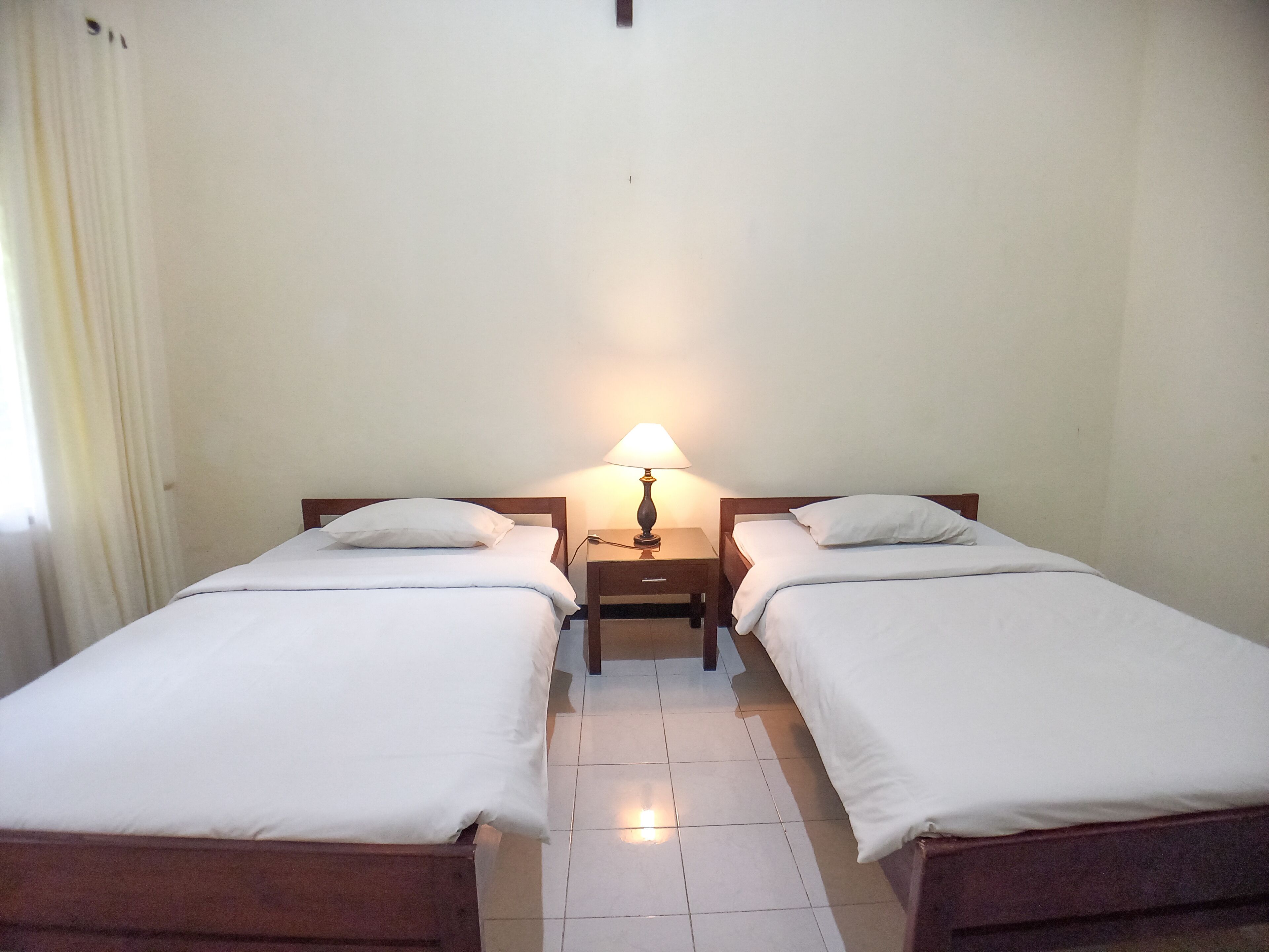 Quarto com duas camas de solteiro, mesa de cabeceira com abajur e janela com cortinas.