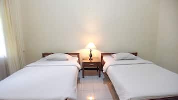 Quarto com duas camas de solteiro, mesa de cabeceira com abajur e janela com cortinas.