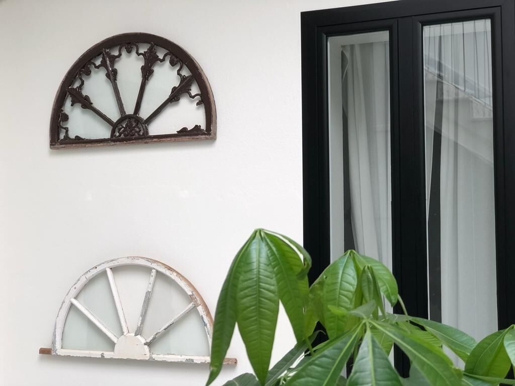 Quarto com parede branca, janela de moldura preta e cortinas leves, além de dois objetos decorativos na parede.