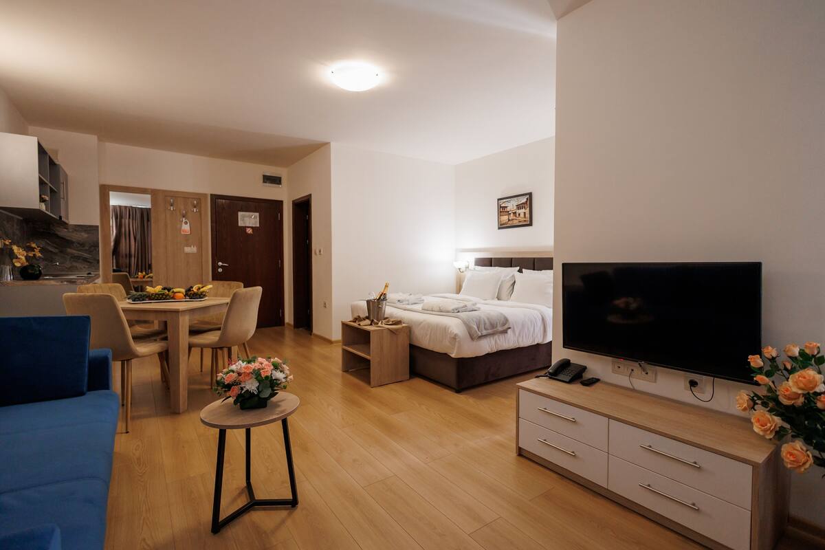 Quarto de hotel moderno com uma cama, televisão, escrivaninha e área de refeições.