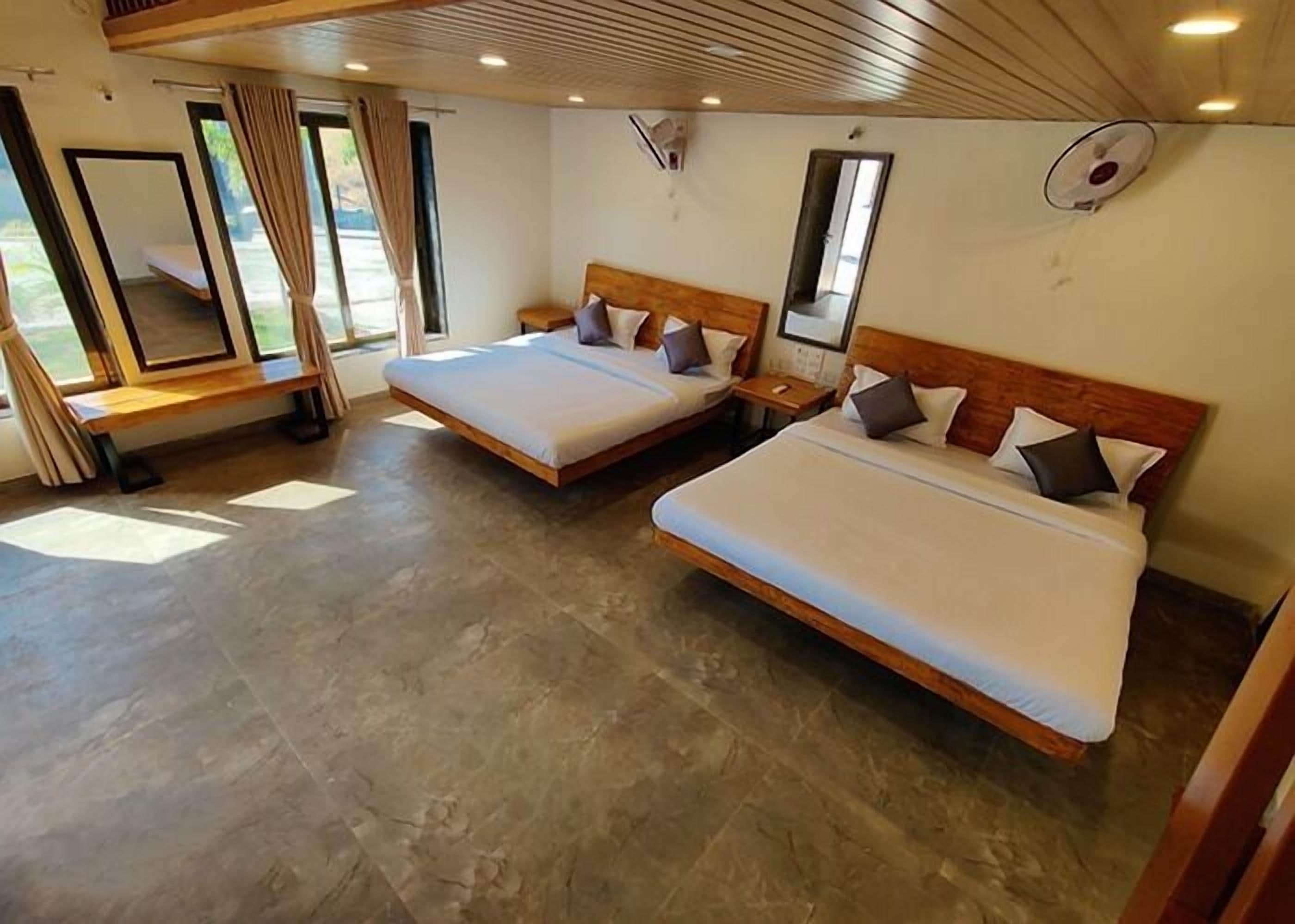 Quarto de hotel com duas camas, um banquinho e uma janela grande.