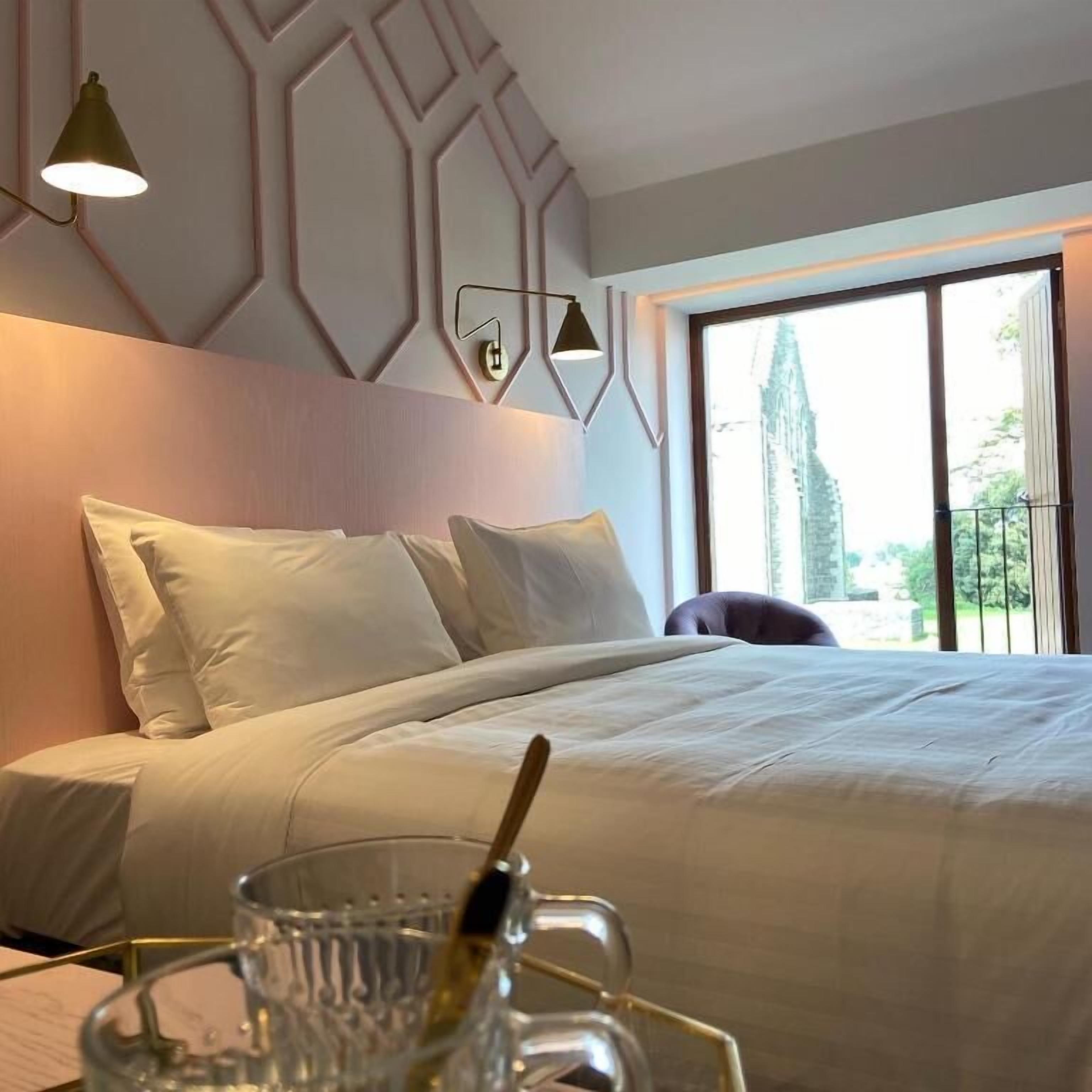 Quarto de hotel com uma cama grande, janela com vista e um painel decorativo na parede.