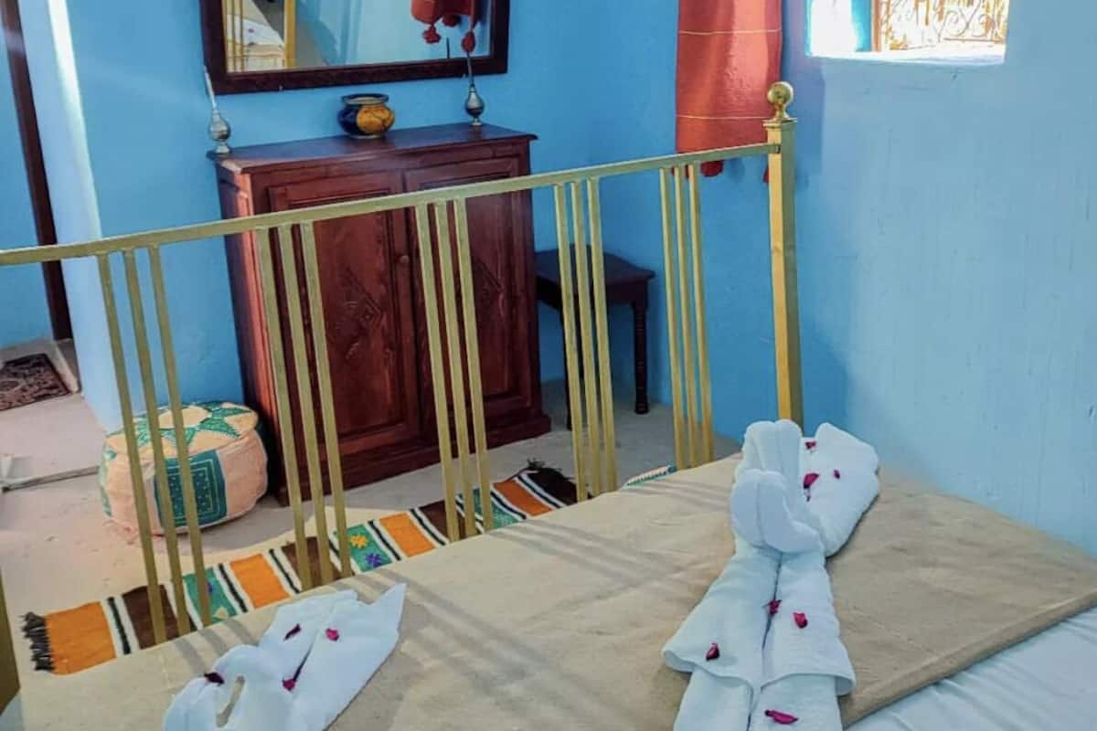 Quarto com uma cama, um armário de madeira, um espelho e uma janela com grades decorativas de ferro.