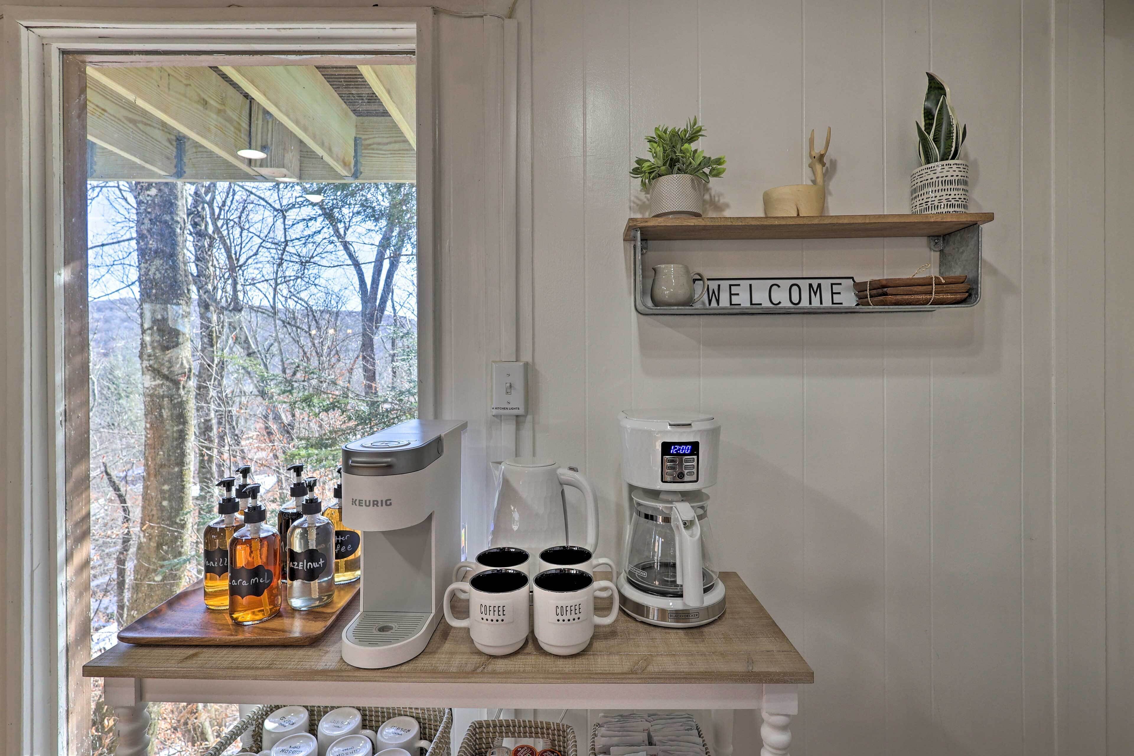 Uma bancada de cozinha com uma cafeteira, canecas e garrafas de xarope.