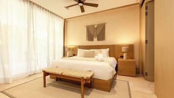 Quarto de hotel moderno com cama grande, cabeceira de madeira, luminárias laterais, um banco e ventilador de teto.