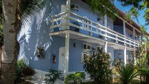 Um edifício de dois andares com varanda, rodeado por plantas tropicais e palmeiras.