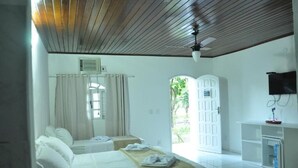 Quarto de hotel com duas camas, ventoinha no teto, televisão e vista para o exterior.