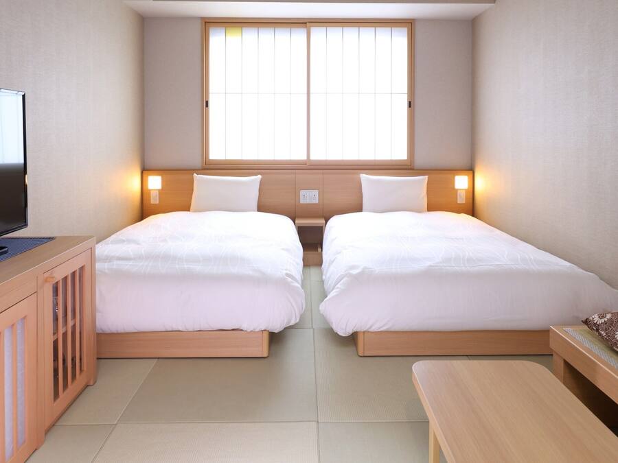 Quarto de hotel com duas camas, televisão e janela com persianas.
