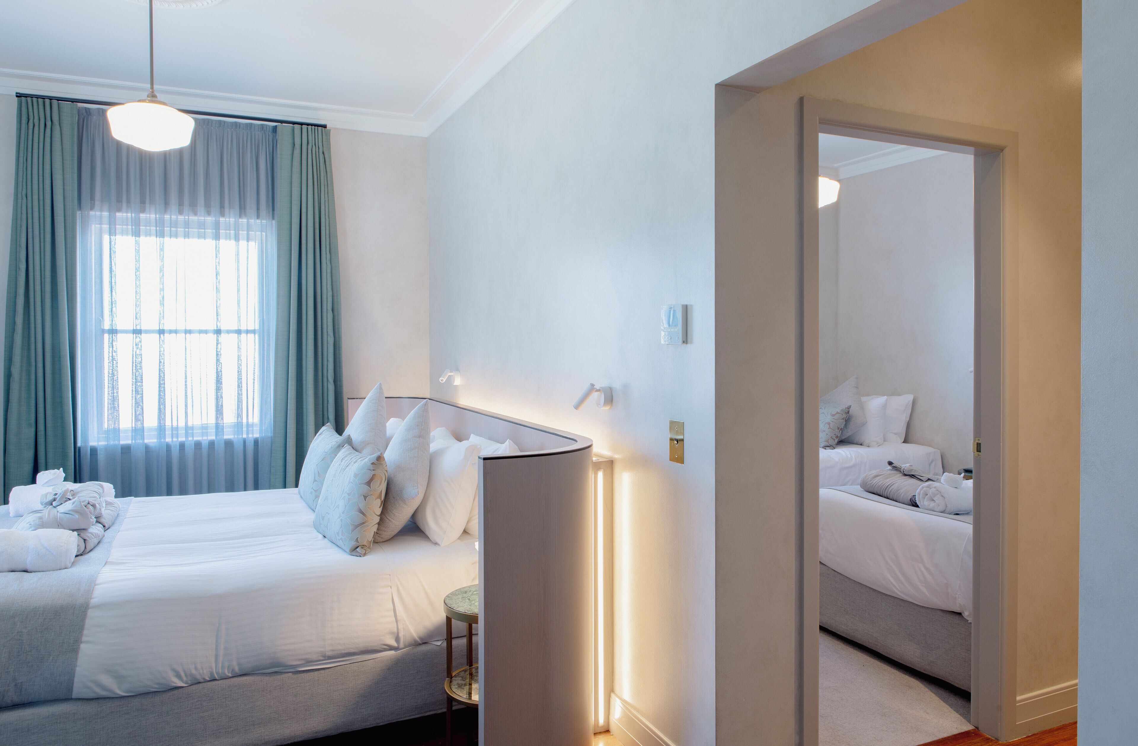 Quarto de hotel com uma cama grande, uma mesa de cabeceira, um espelho e uma janela com cortinas.