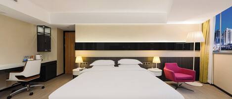 Quarto de hotel moderno com cama grande, escrivaninha, cadeira e vista para a cidade.