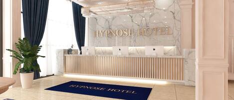 Uma área de recepção de hotel com parede de mármore, balcão de atendimento e planta em vaso.